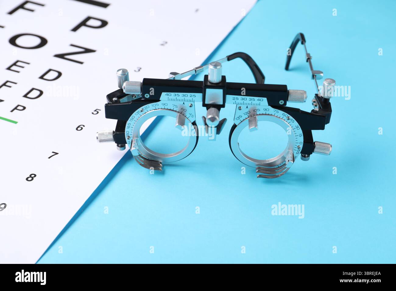 Vision test chart and trial frame on light blue background, closeup ...