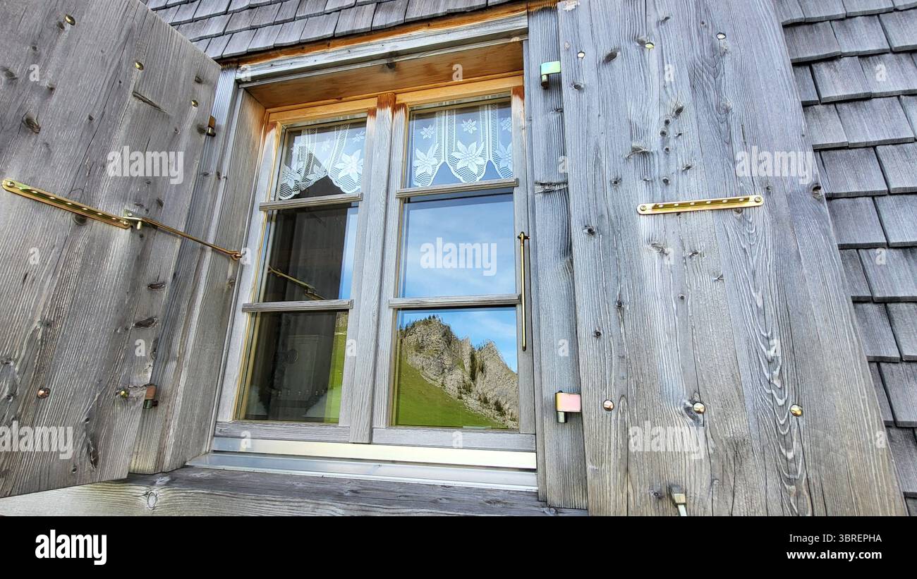 window with shutters and window reflection with blue sky of a mountain ...