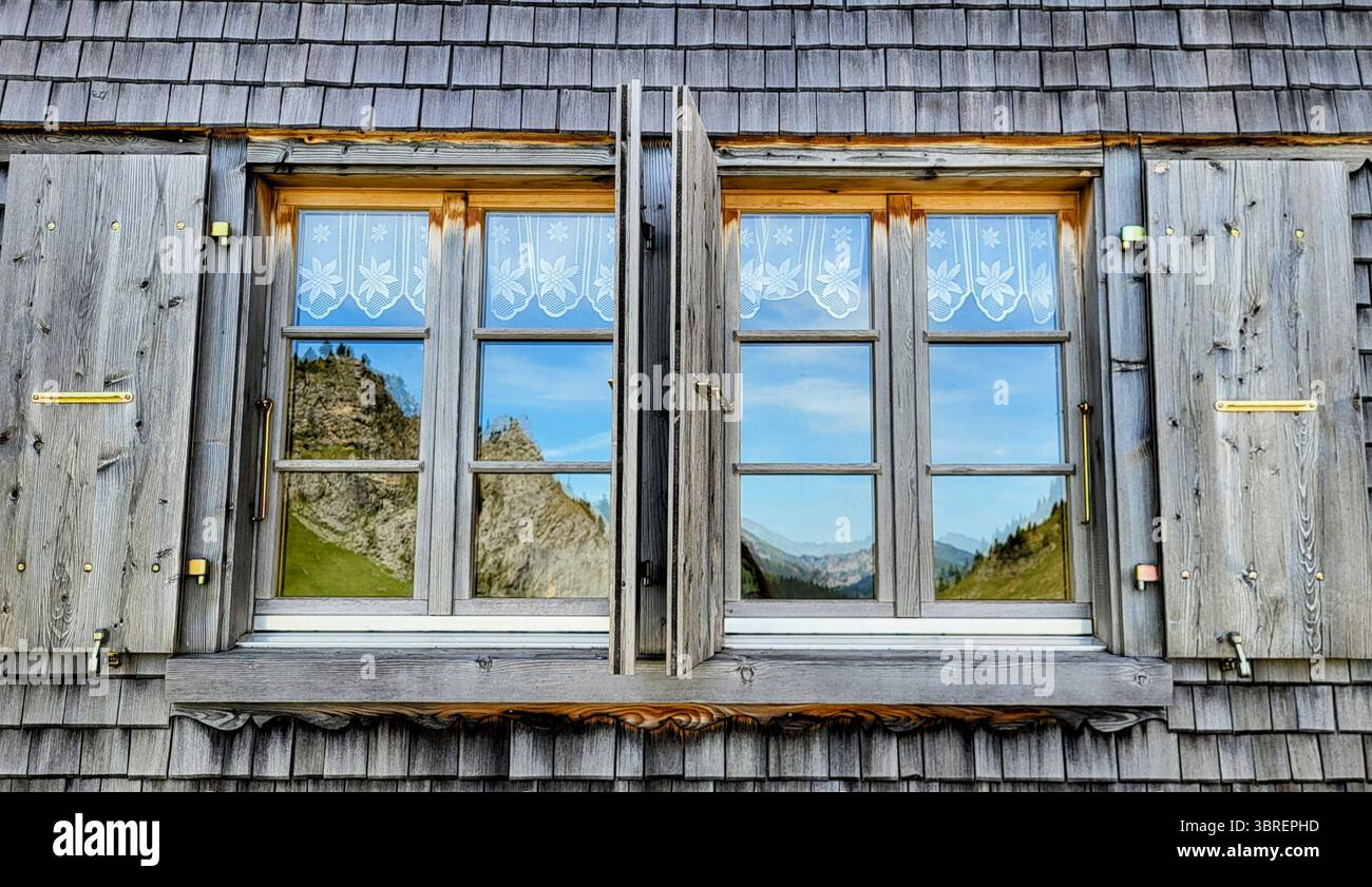 window with shutters and window reflection with blue sky of a mountain ...