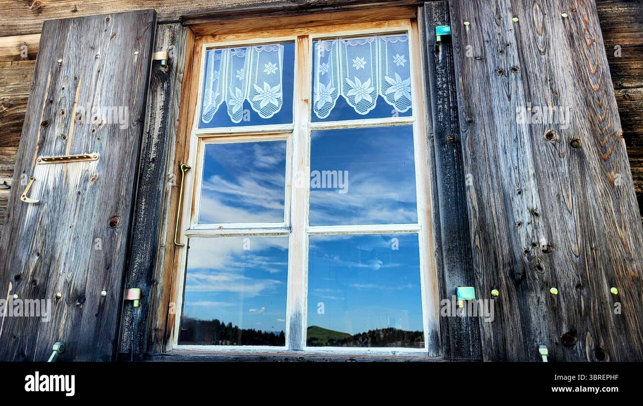 window with shutters and window reflection with blue sky of a mountain ...