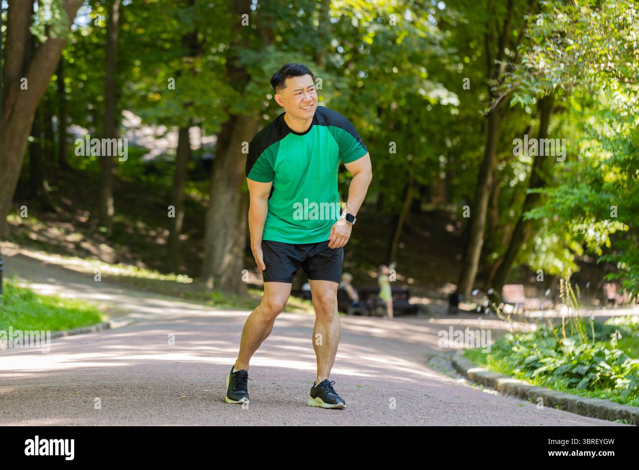 Japanese runner athlete with muscle pain in sunny park. Man massaging ...