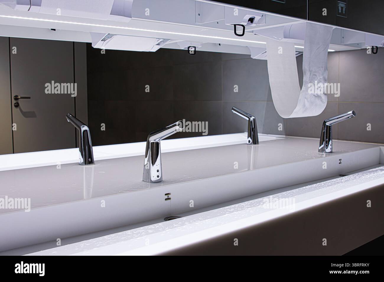 Interior of a modern public restroom featuring a long white sink with ...