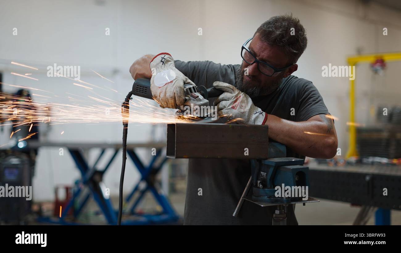 Metalworker using angle grinder, creating sparks while working on steel ...