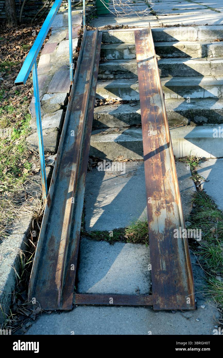 Weathered metal ramp sits neglected alongside cracked pavement and ...