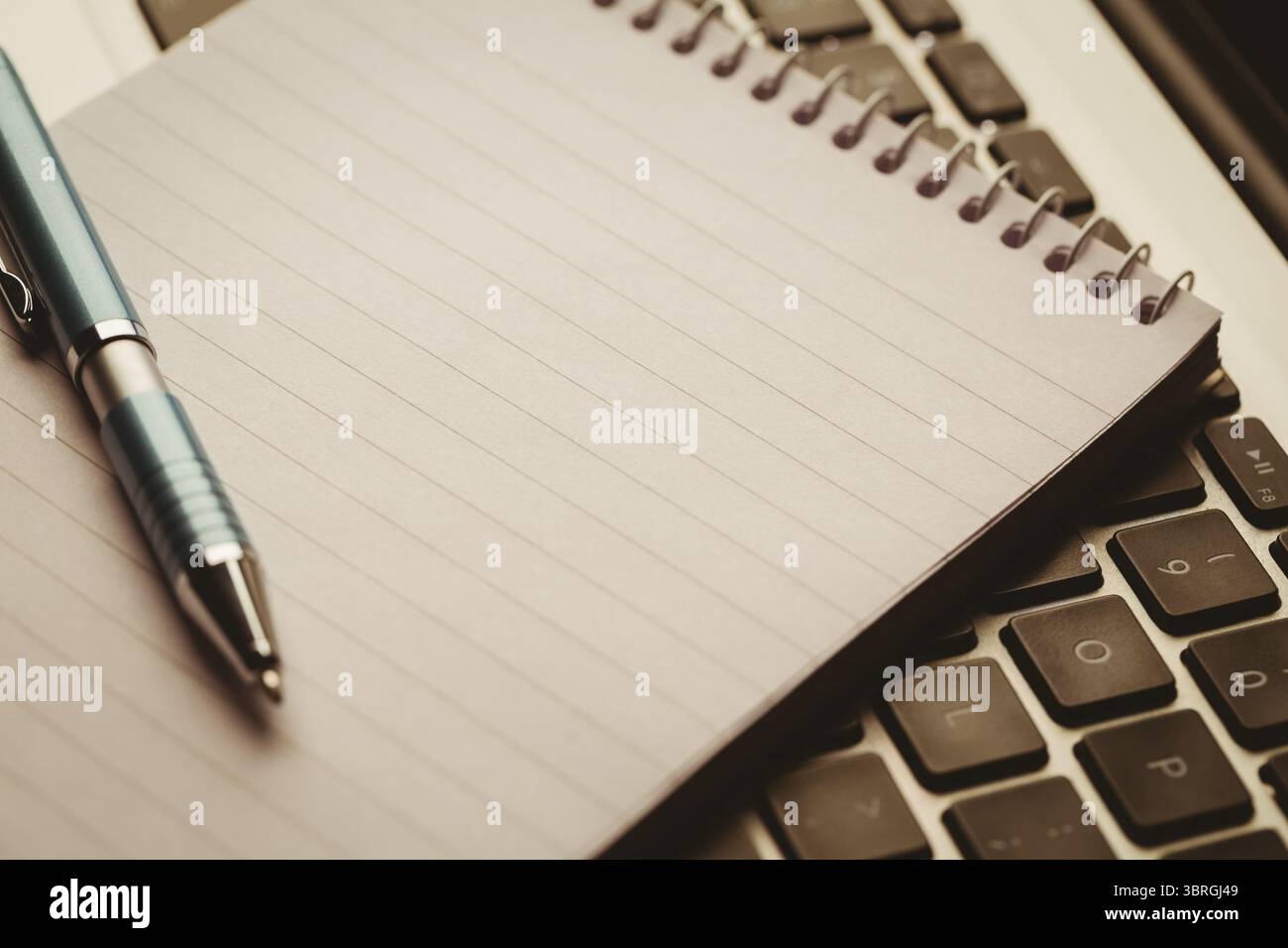 Spiral-bound notebook and ballpoint pen are resting on laptop keyboard ...
