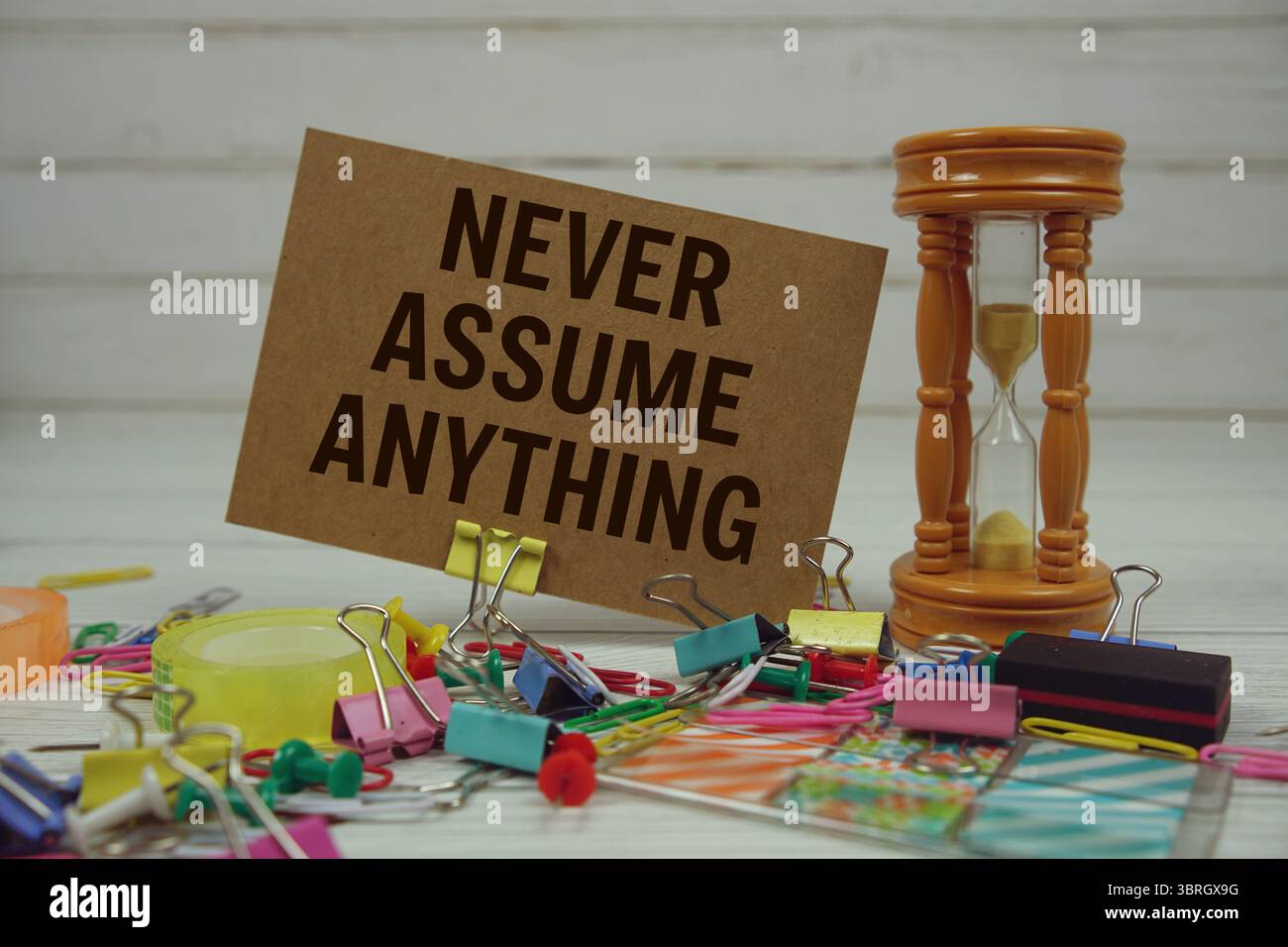Never Assume Anything text on paper card with hourglass and stationary ...