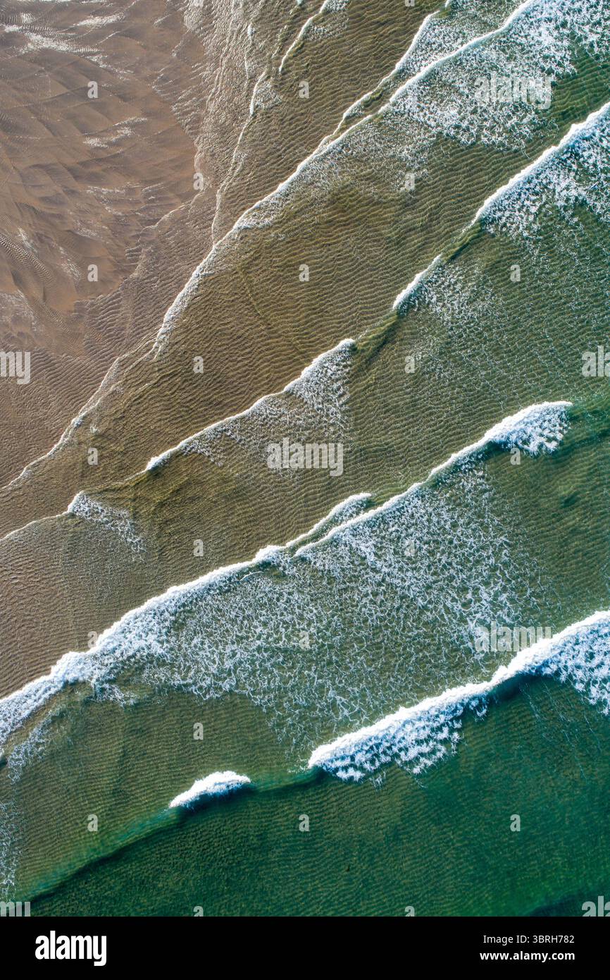 aerial top-down view of powerful ocean waves breaking on a sandy beach ...
