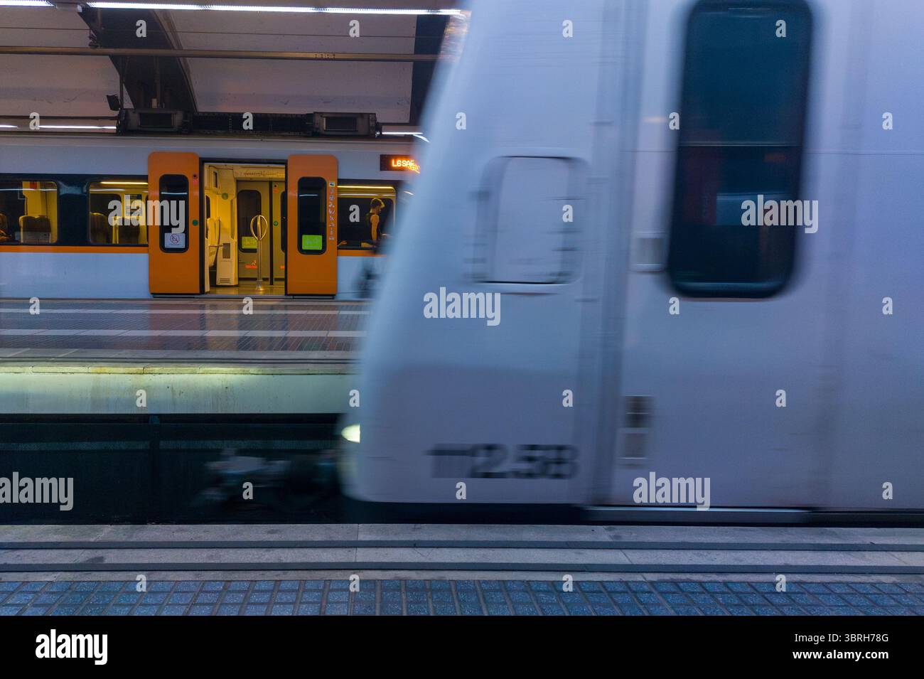 White train leaving station with open doors orange train passing by ...