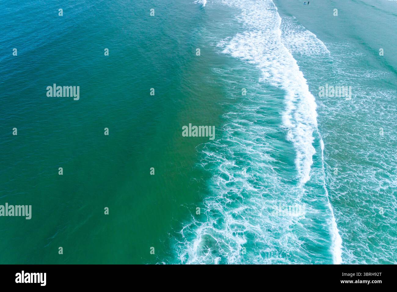 aerial view of a wide turquoise ocean with a long, breaking wave and ...