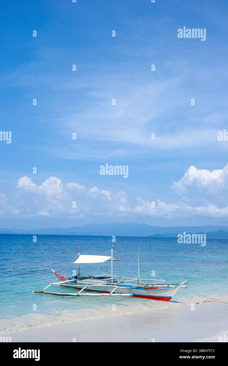A traditional Filipino outrigger boat or bangka is anchored on a quiet ...