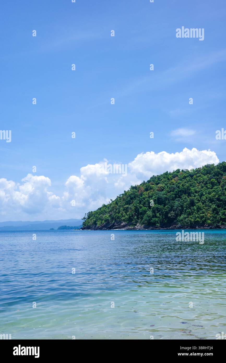 A lush tropical island extends into the calm, and the water transitions ...