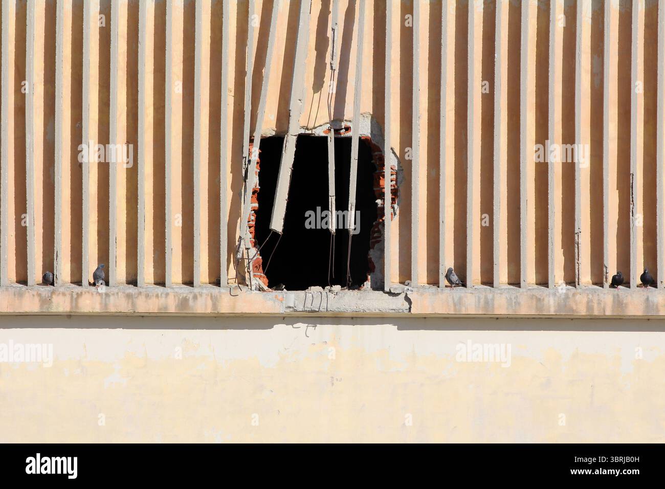 A damaged exterior wall with vertical concrete beams features a large ...