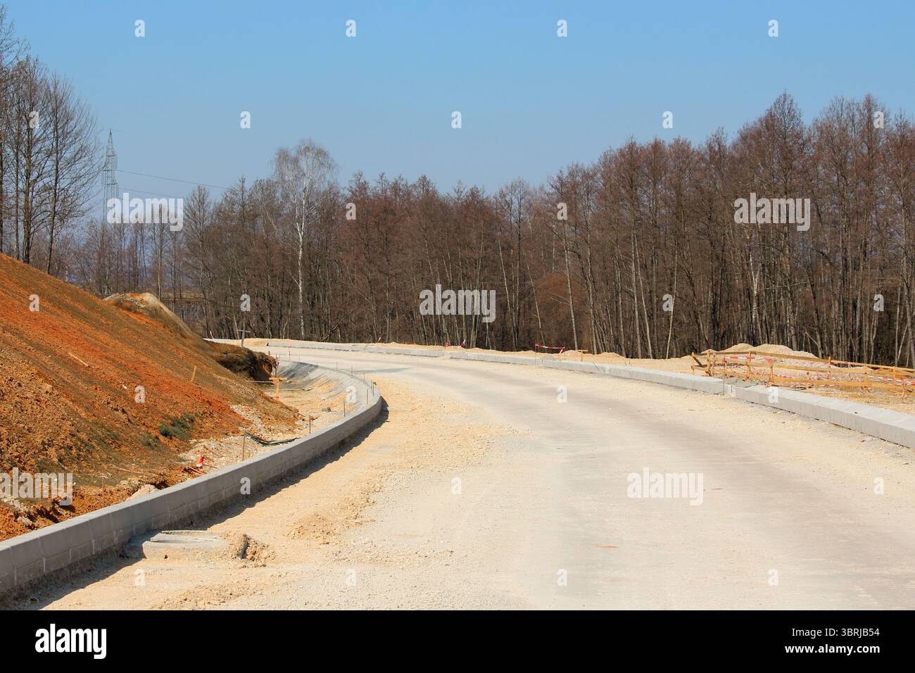 A newly graded gravel road curves gently through a forest edge ...