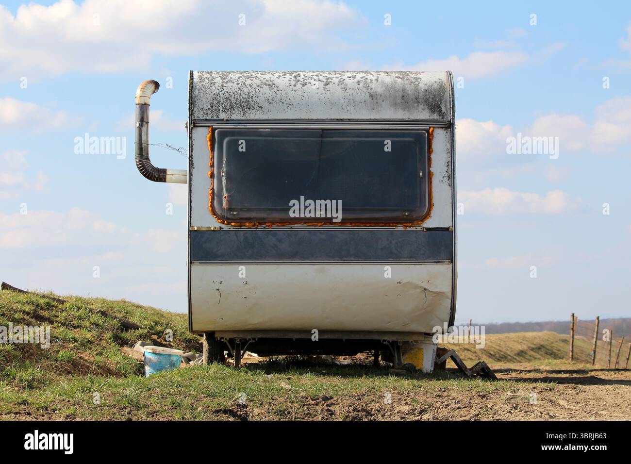 A neglected caravan with a rust-stained window and bent chimney pipe ...