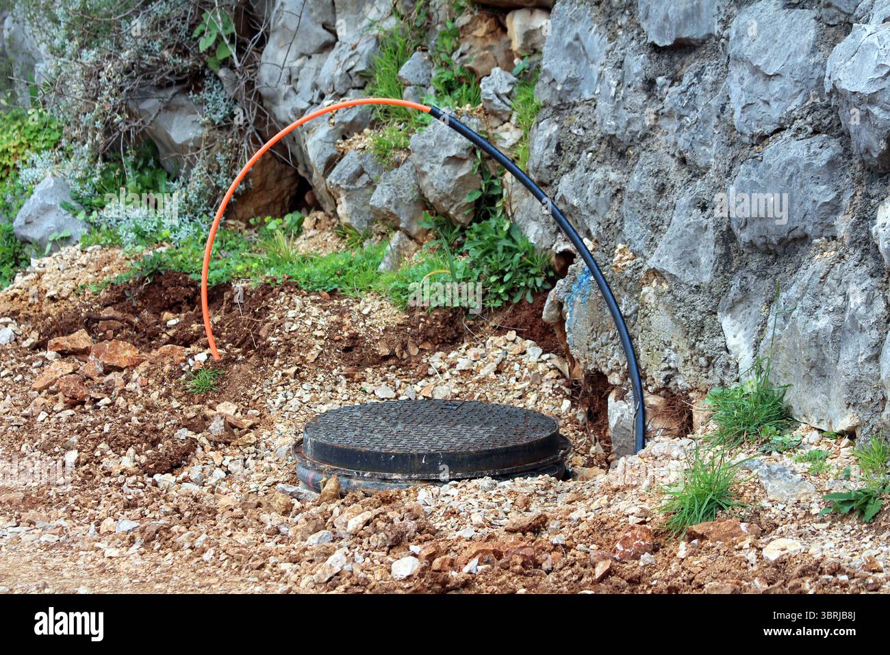 A round utility manhole cover sits partially buried in gravel and soil ...