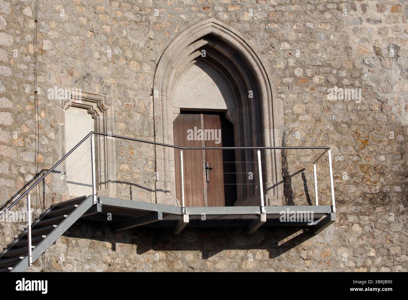 A pointed Gothic arched doorway with wooden doors opens onto a modern ...