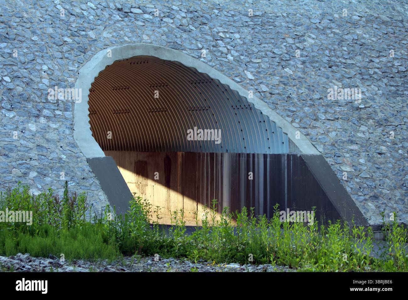 A uniquely shaped tunnel entrance is set in a sloped stone wall ...