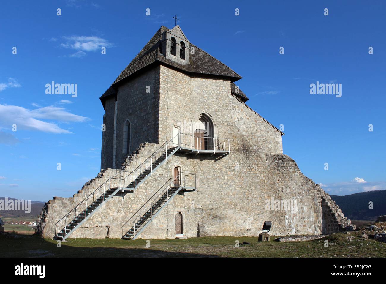 A small medieval church with a bell gable and steep roof sits atop a ...