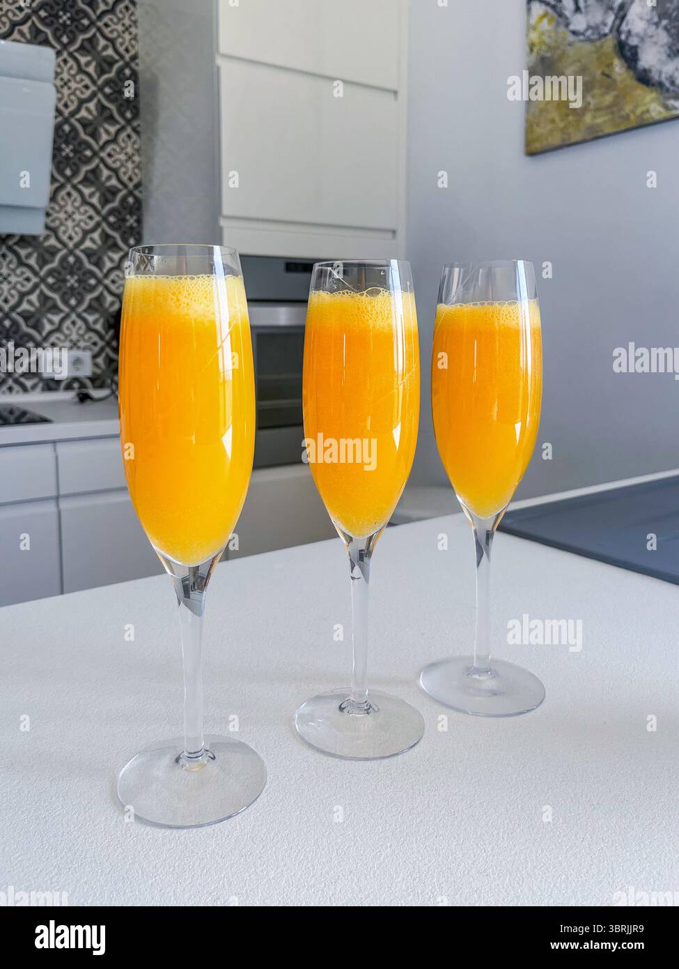 Three stylish champagne glasses filled with bright orange juice are ...