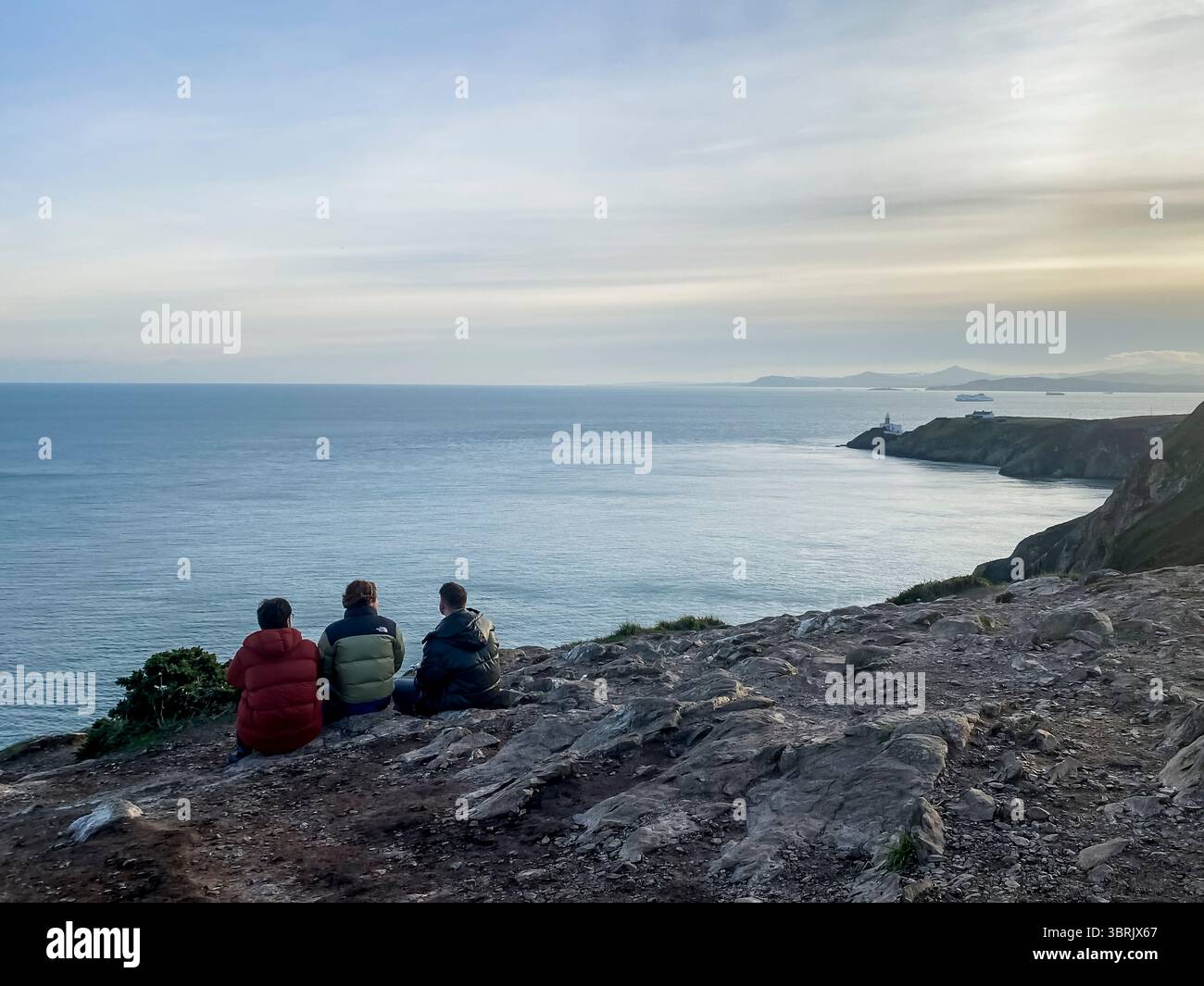 Three guys look the lighthouse on the Howth Cliff Walk of Howth ...