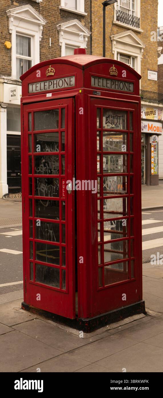 A traditional red telephone booth stands on a sidewalk in front of a ...