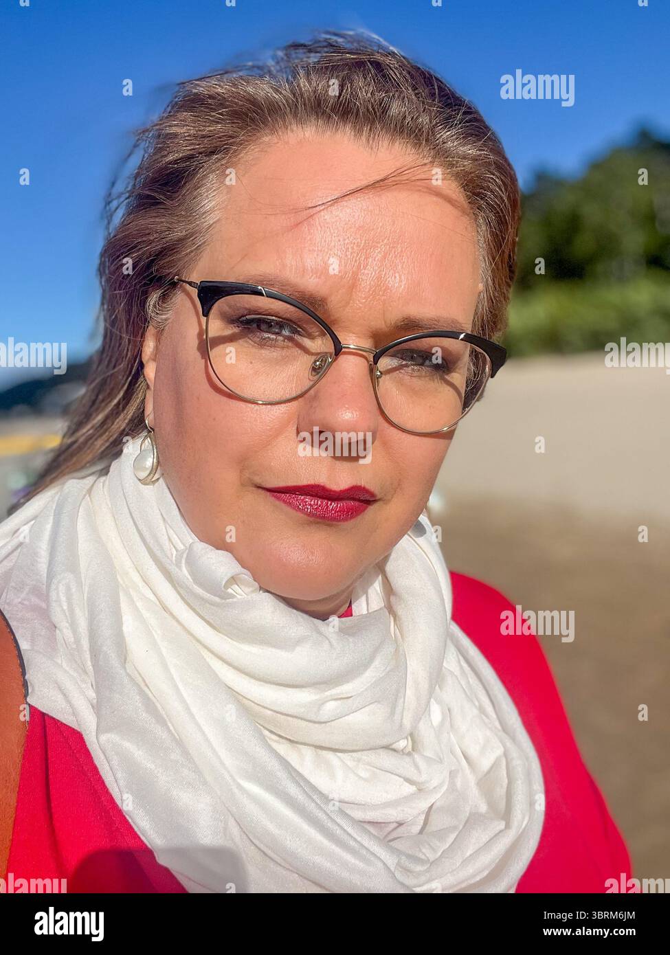 Woman with glasses and a white scarf poses outdoors, wearing a red ...