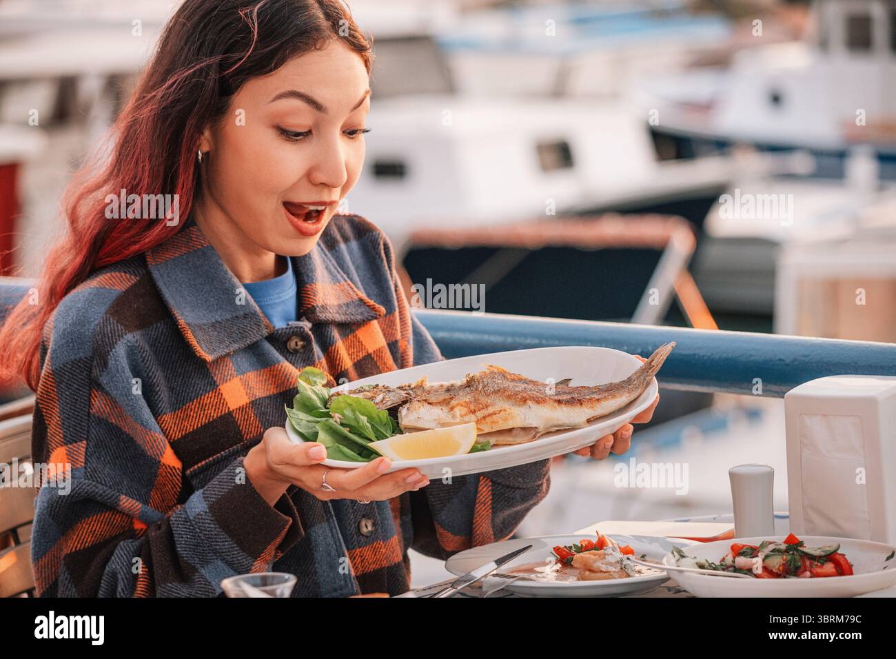 Customer showing grilled fish dish in outdoor restaurant with marina ...