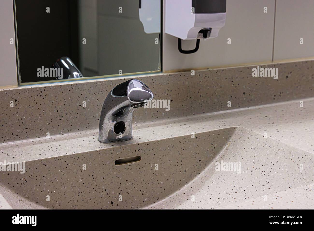 Modern sensor faucet mounted on a gray stone basin, mirror, and soap ...