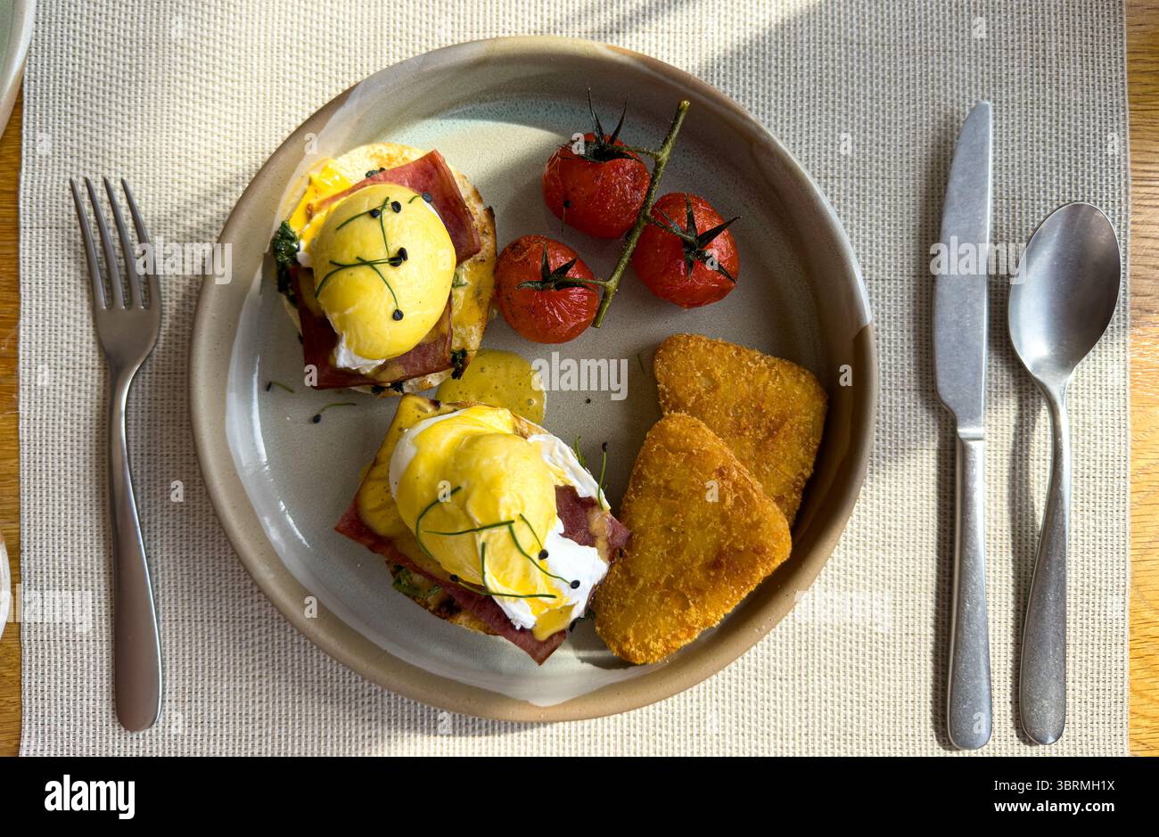A plate with eggs Benedict, roasted tomatoes, and hash browns, placed ...