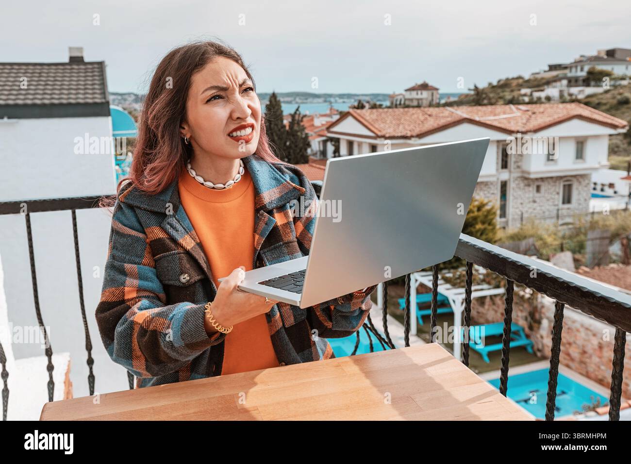 Young frustrated woman looking up and screaming while holding laptop ...