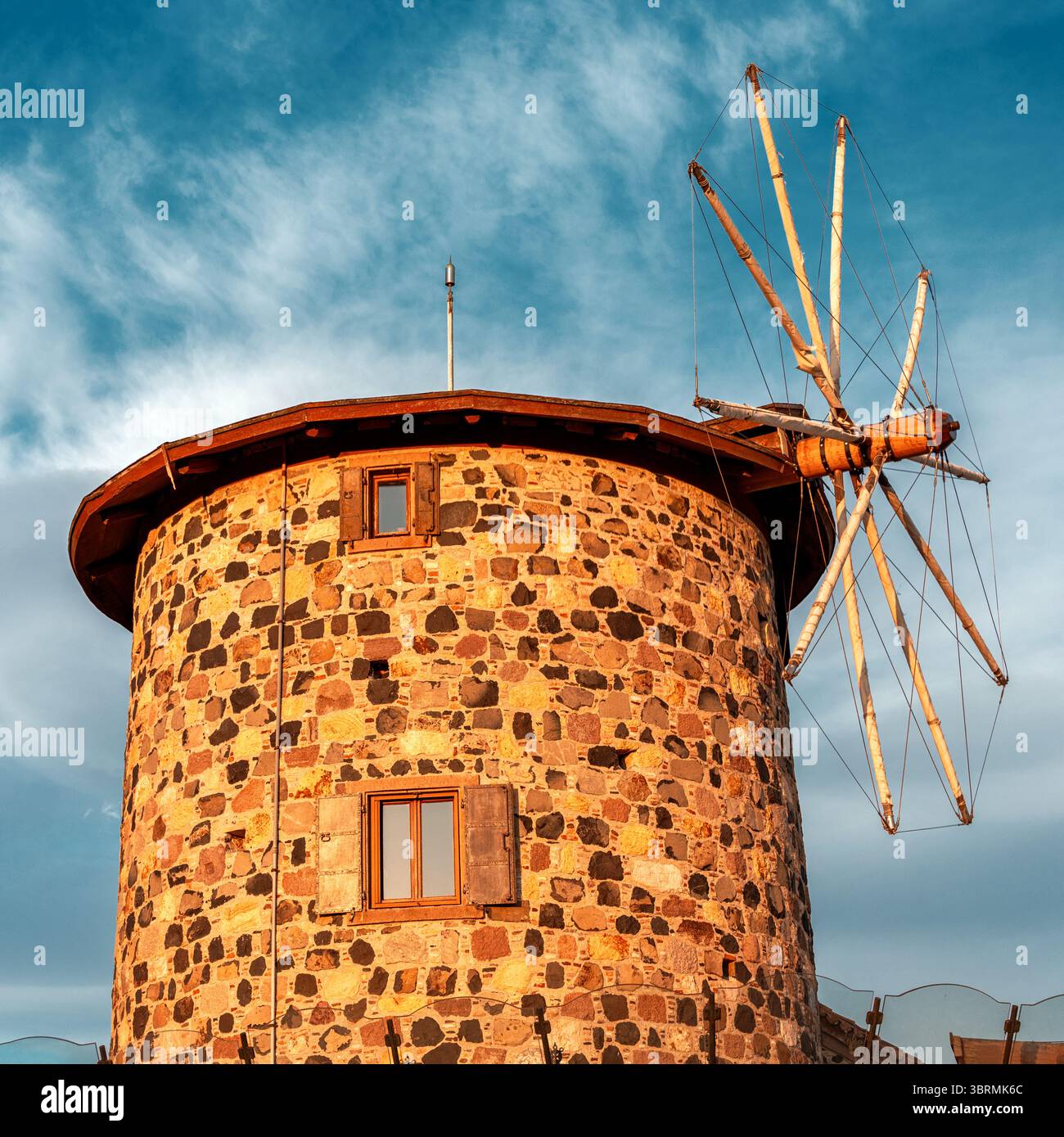 Warm sunlight illuminates a historic stone windmill, its wooden sails ...