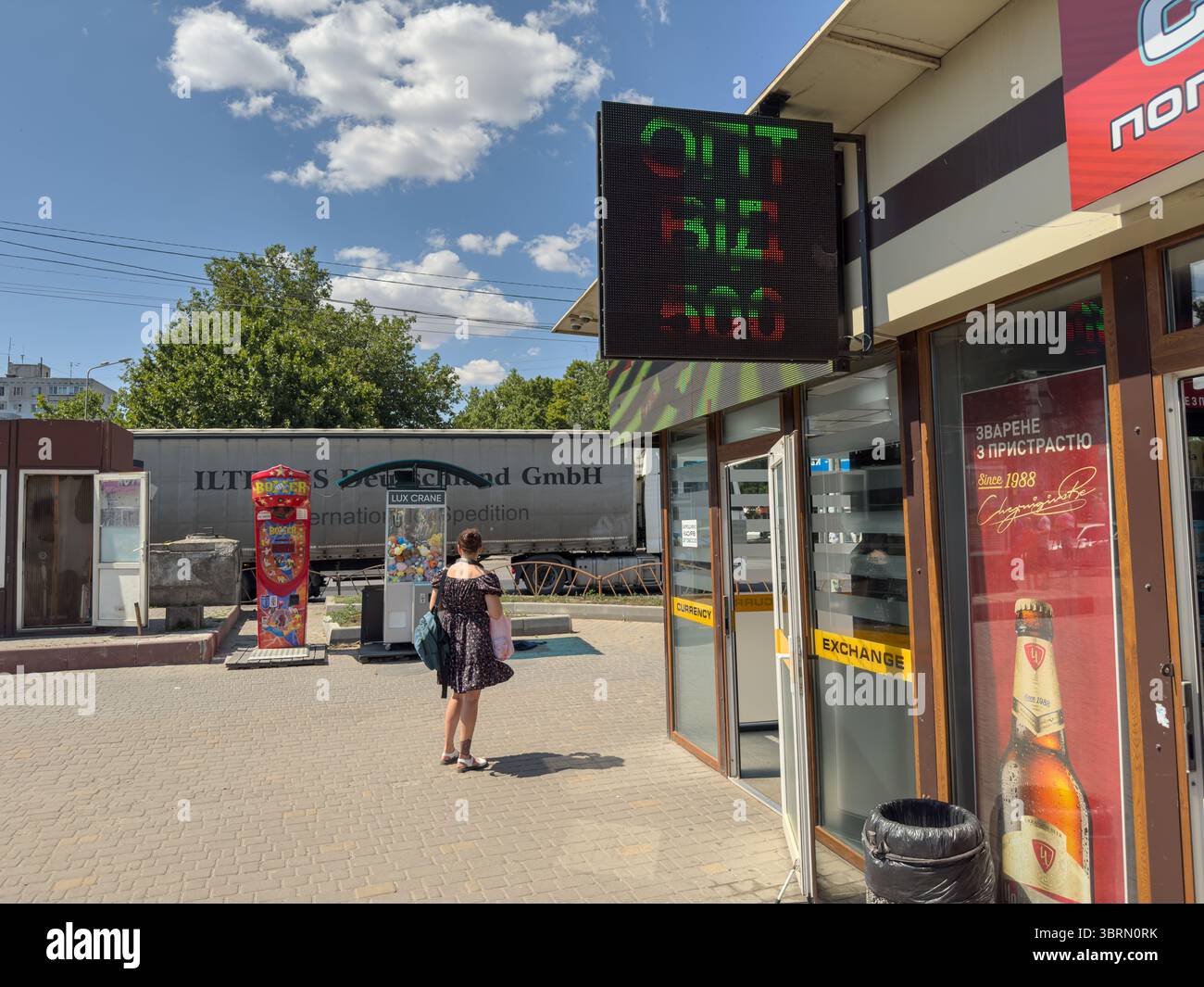 woman walks past a currency exchange with a bright digital board ...
