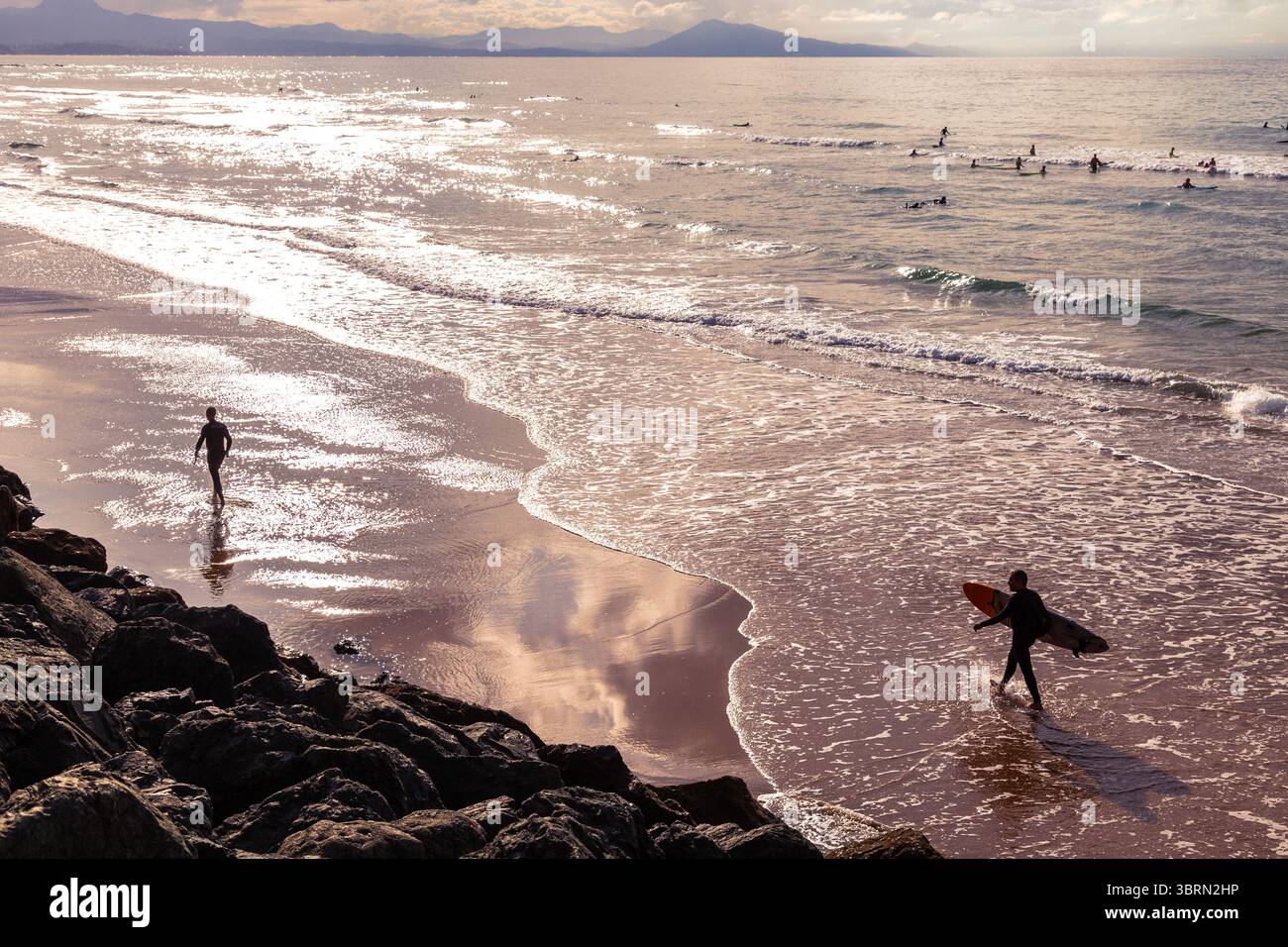Surfer walking down Côte des Basques surfing beach at sunset in ...