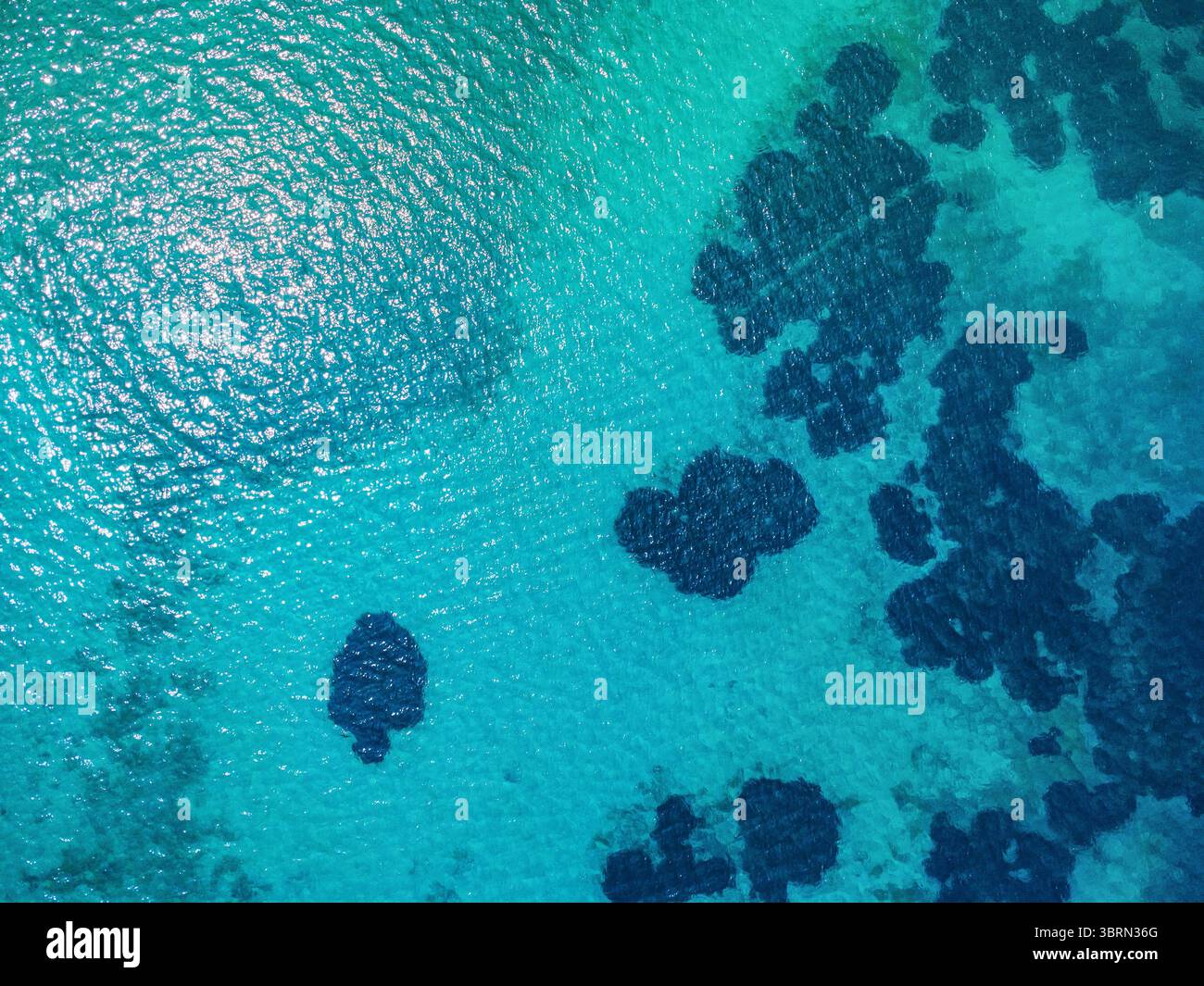 Turquoise water surface with dark seabed formations visible from above ...