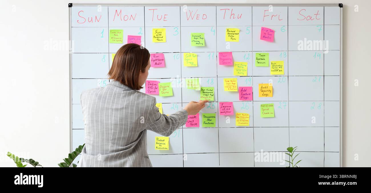 Young businesswoman sticking notes with plans on whiteboard in office ...