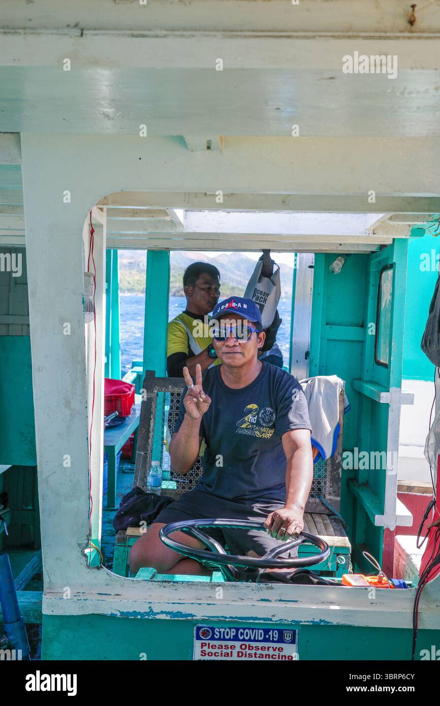 A Filipino guy is sunglasses and cap, controlling a ferry boat from ...