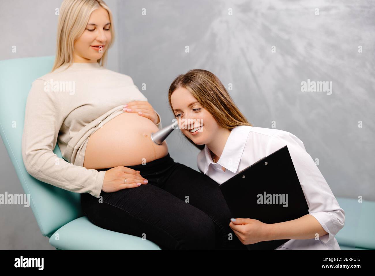 A gynecologist leans a stethoscope to a pregnant woman's belly and ...