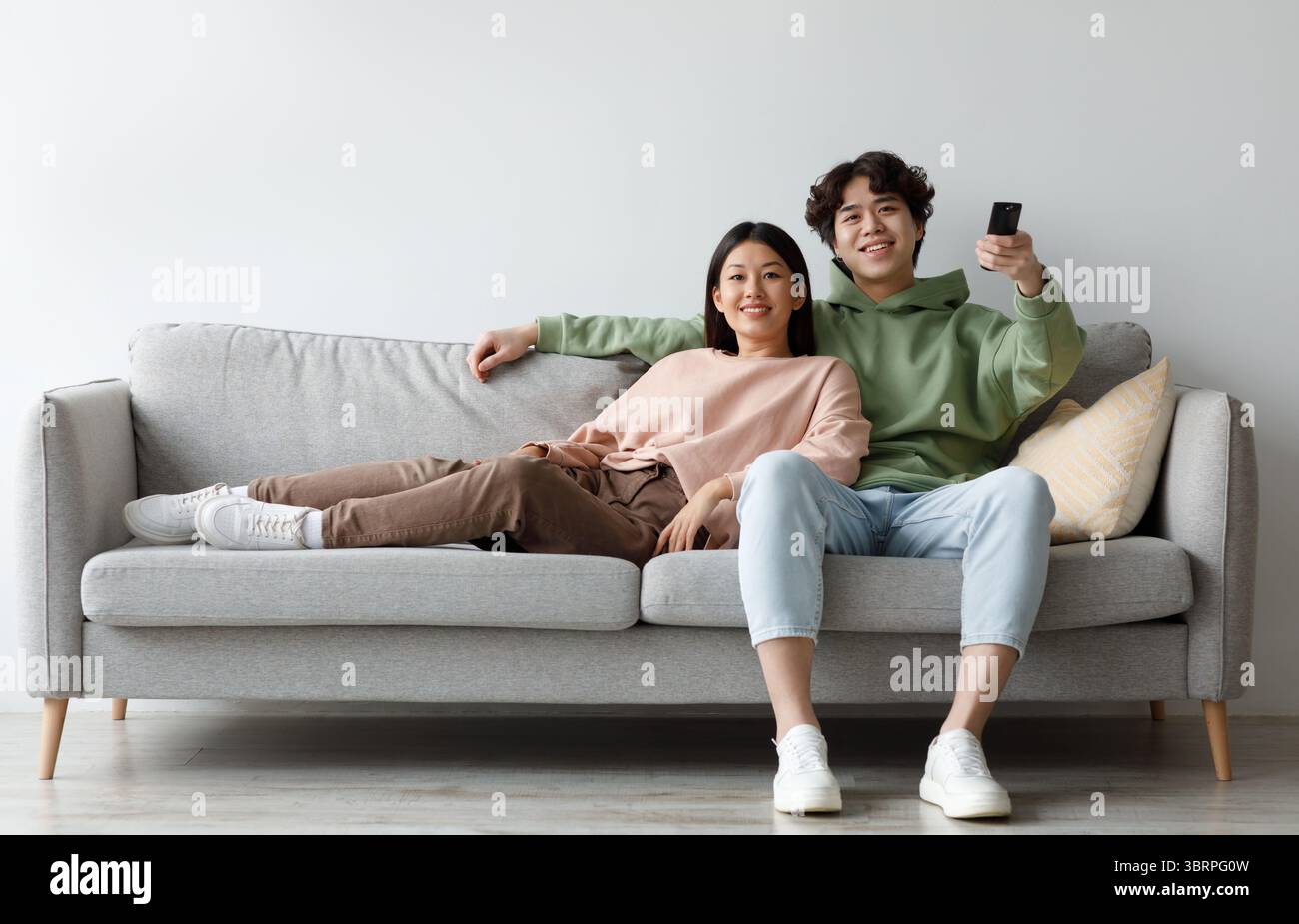 Young Asian couple relaxing on sofa, watching TV, switching channels ...
