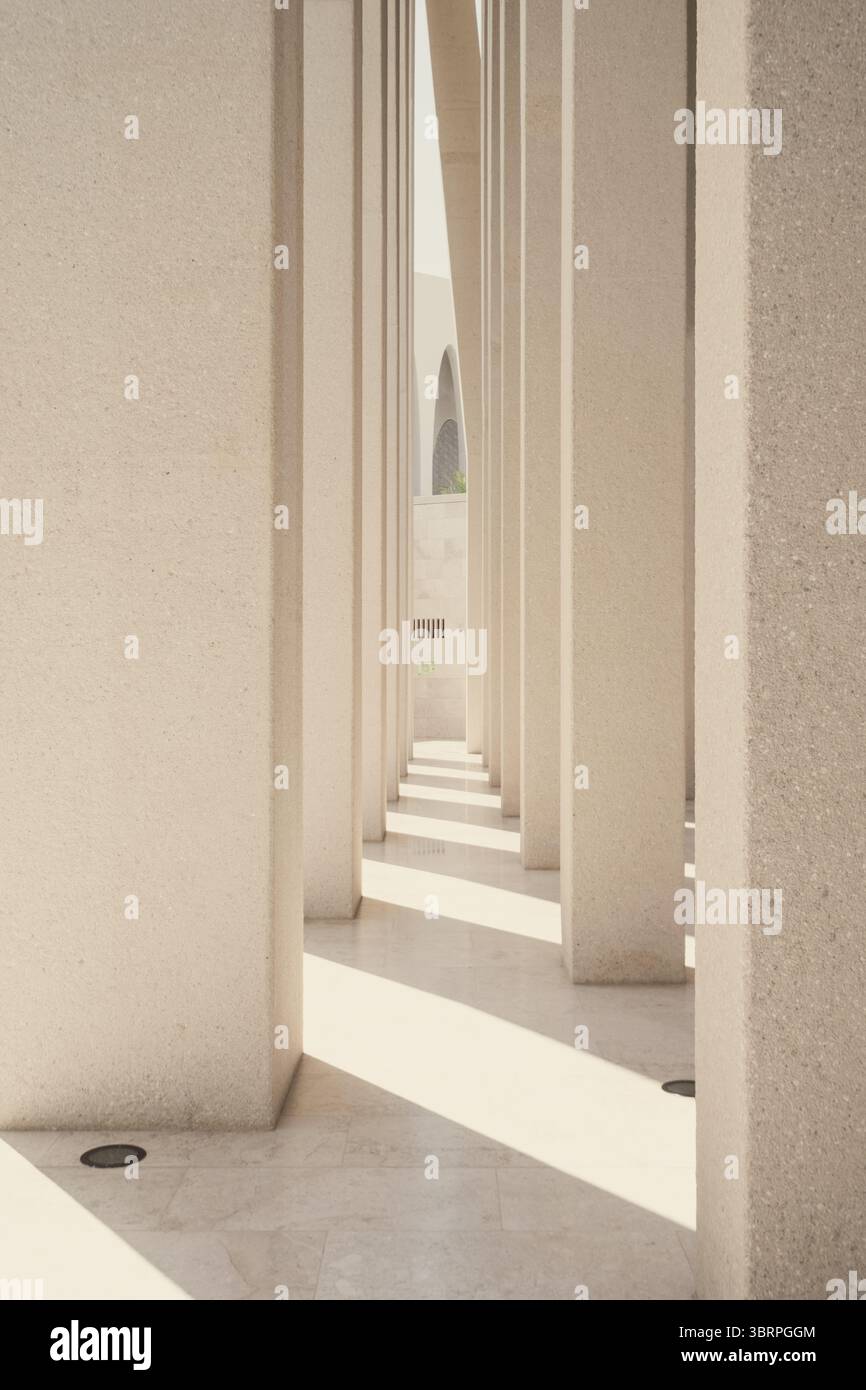 An architectural corridor with tall concrete pillars, casting geometric ...