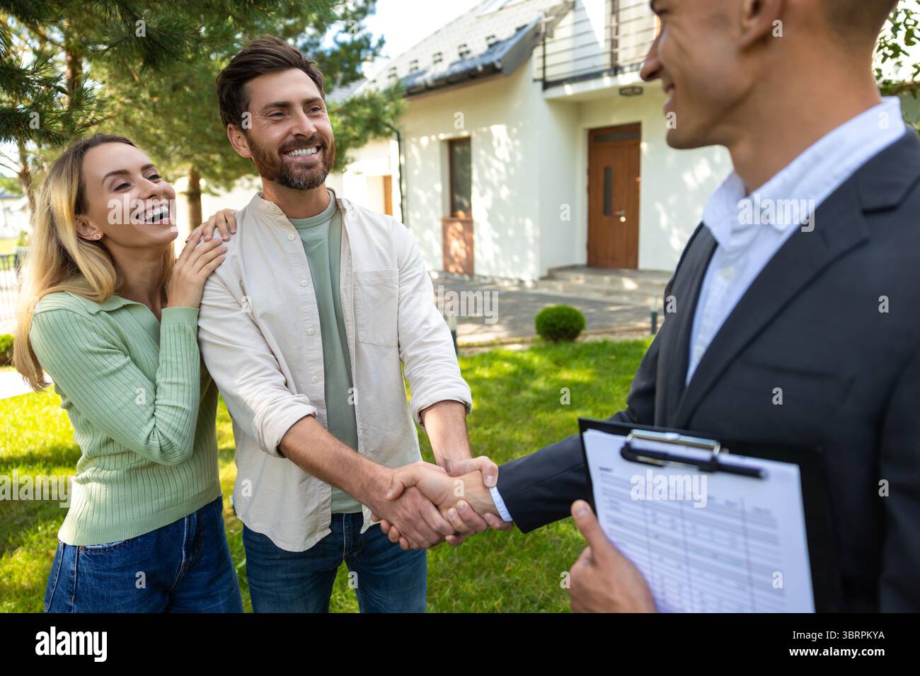 Happy couple greeting agent at new house in suburban setting Stock ...