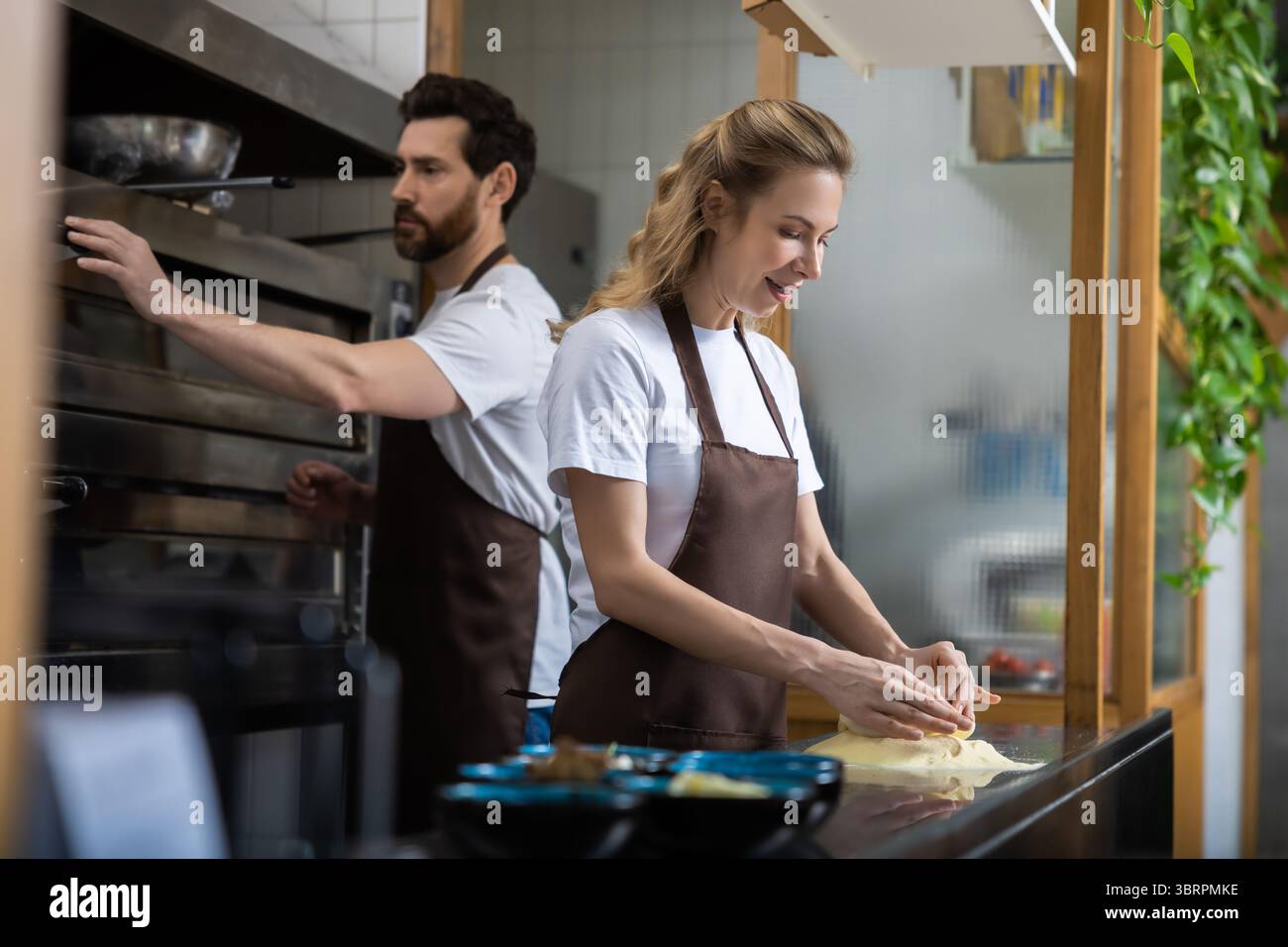 Male and female bakers working together in a bakery kitchen, discussing ...