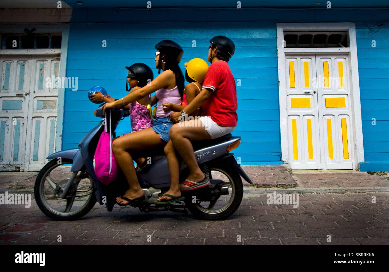 Four people ride on a moped through the streets on Isla Mujeres, Mexico ...