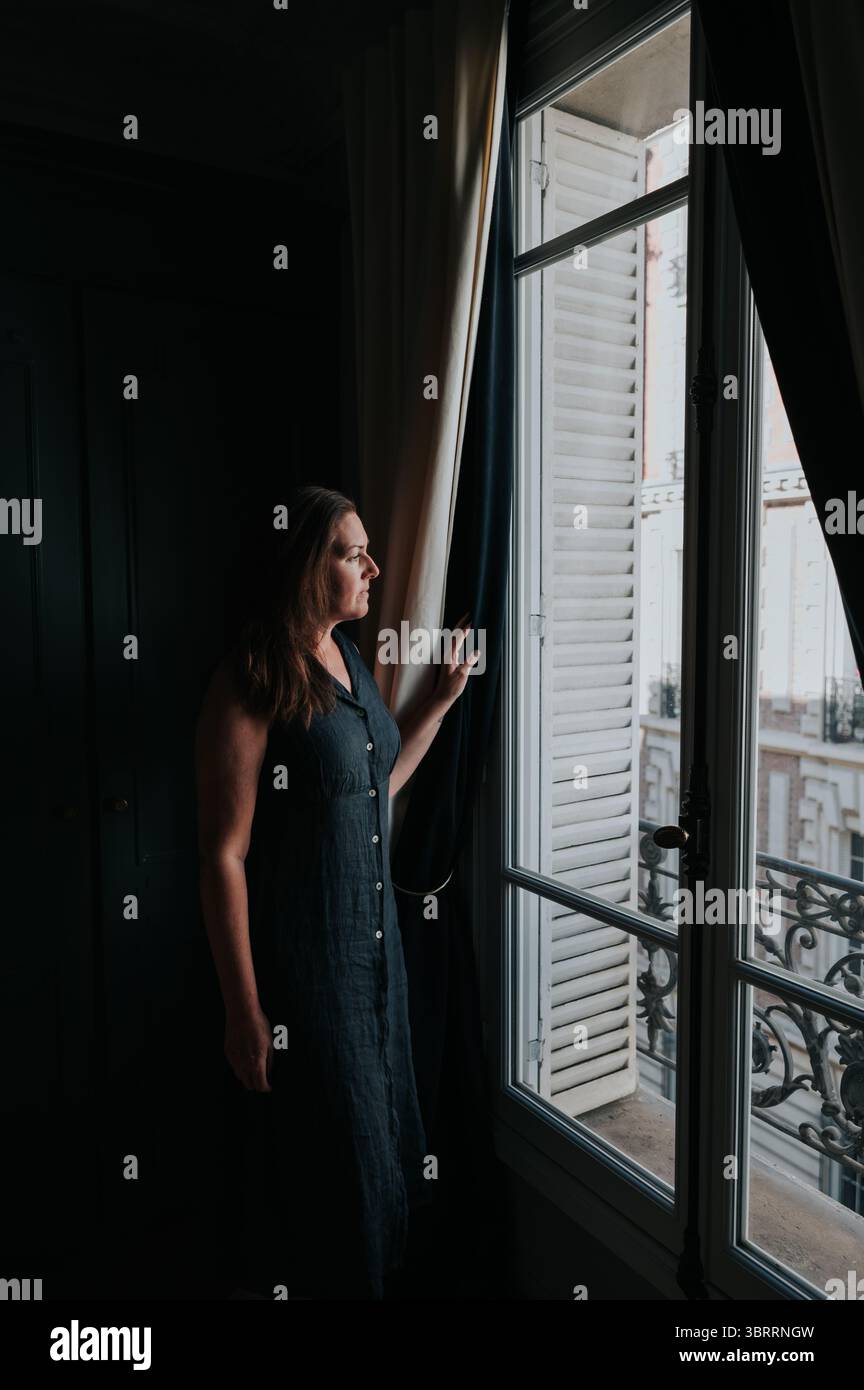 Woman looking out of tall shuttered window in Paris apartment Stock ...