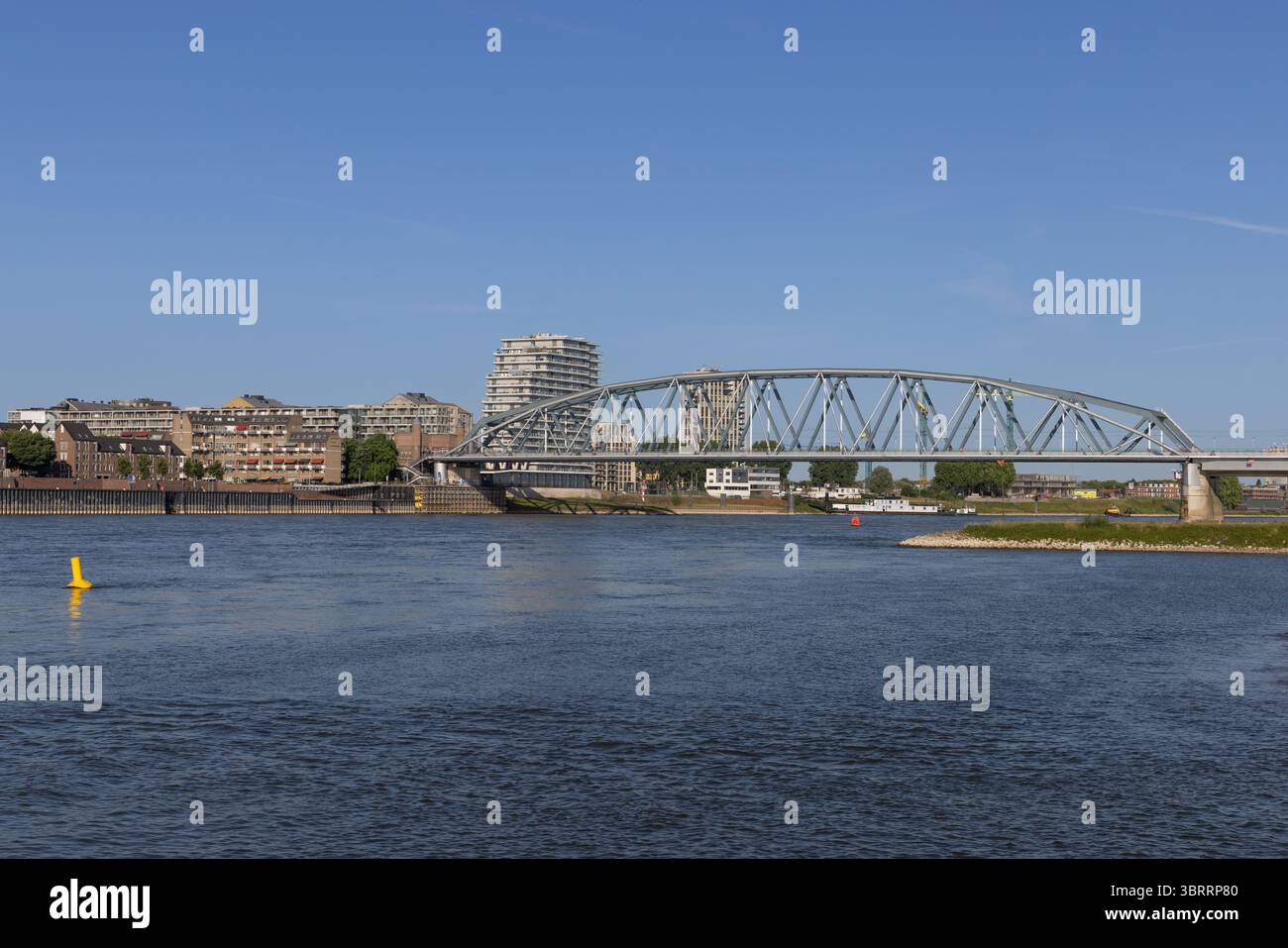 The robust Nijmegen Railway Bridge arcs across the Waal River on a ...