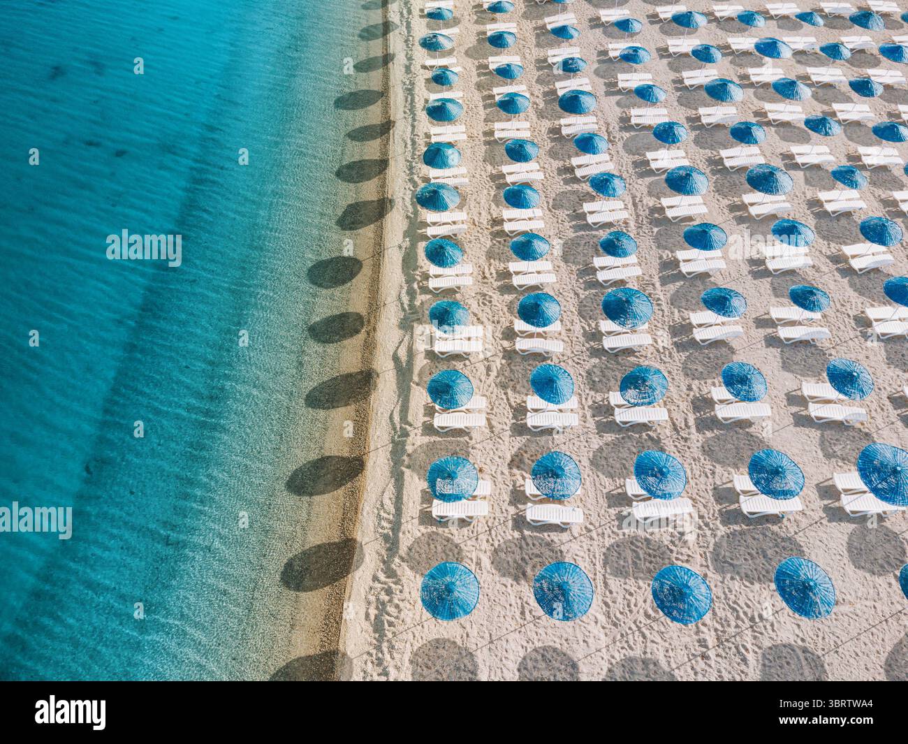 Aerial view of rows of blue beach umbrellas and white deckchairs ...