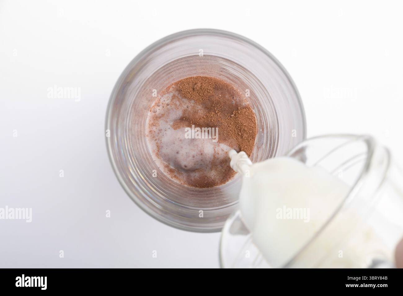 making cocoa drink in glass, adding milk into coca power from above on ...