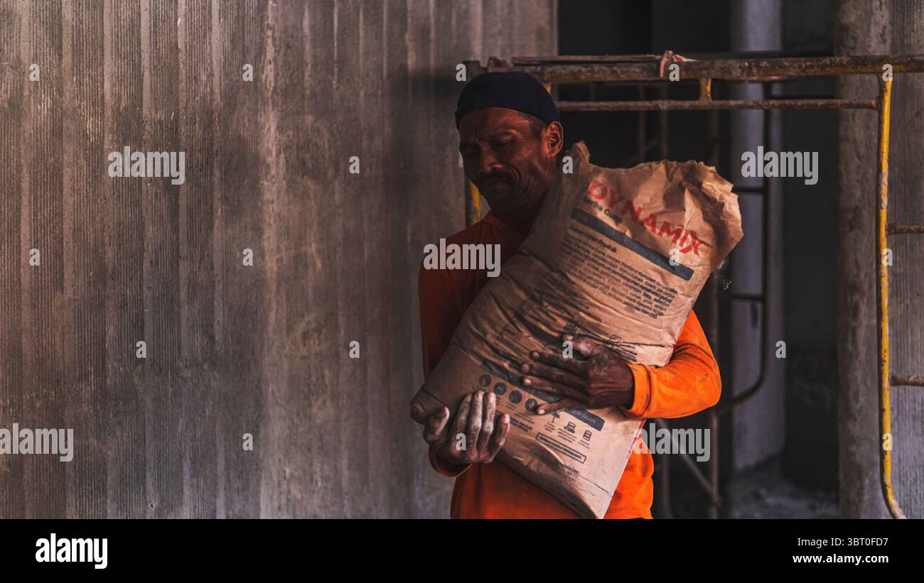 A male worker lifts a heavy cement bag at a construction site ...