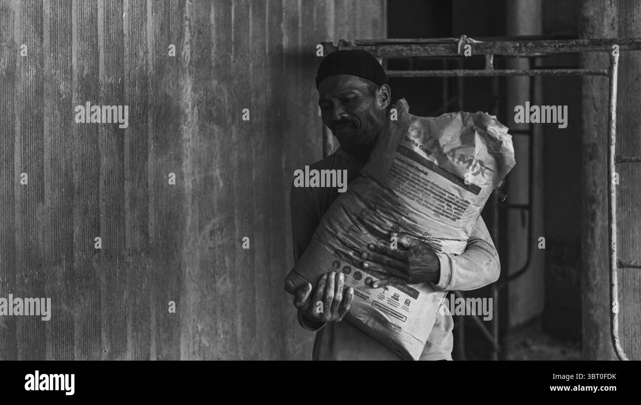 A male worker lifts a heavy cement bag at a construction site ...