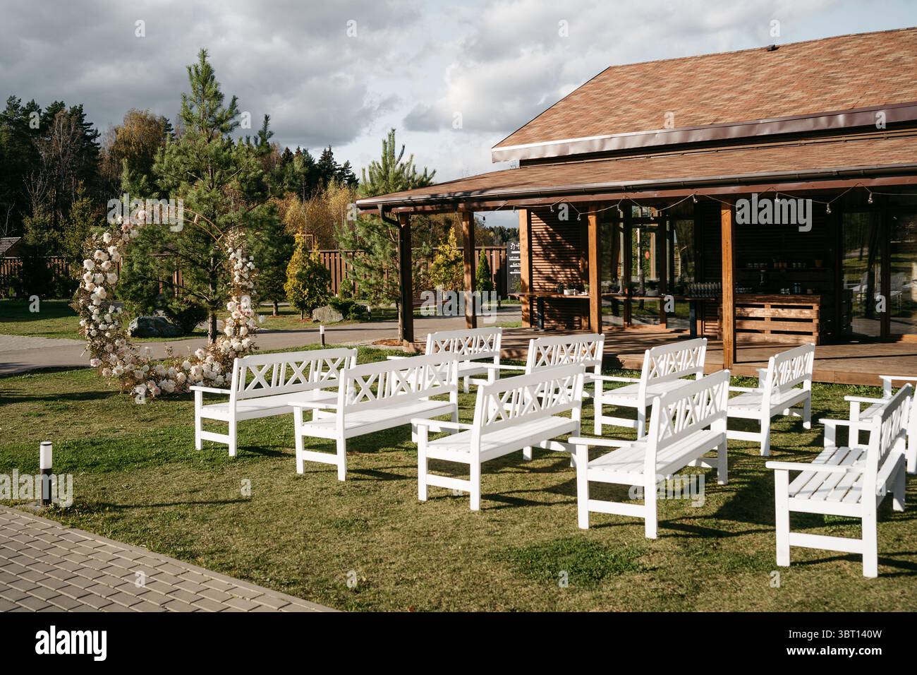 An outdoor wedding venue features white benches facing a floral arch in ...