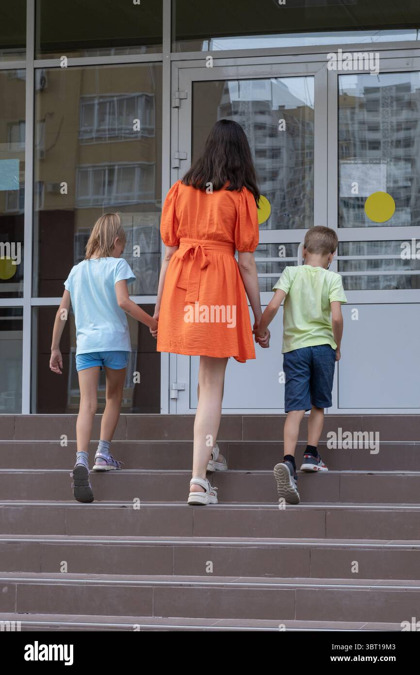 Woman with two children walking upstairs to school building entrance ...